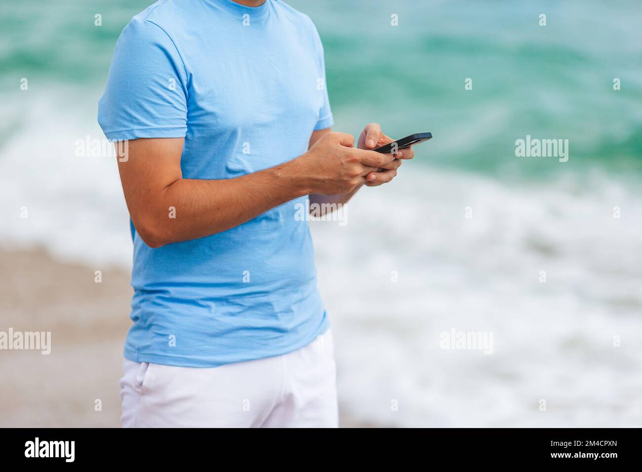Young man using mobile phone while walking on the beach. Closeup ...