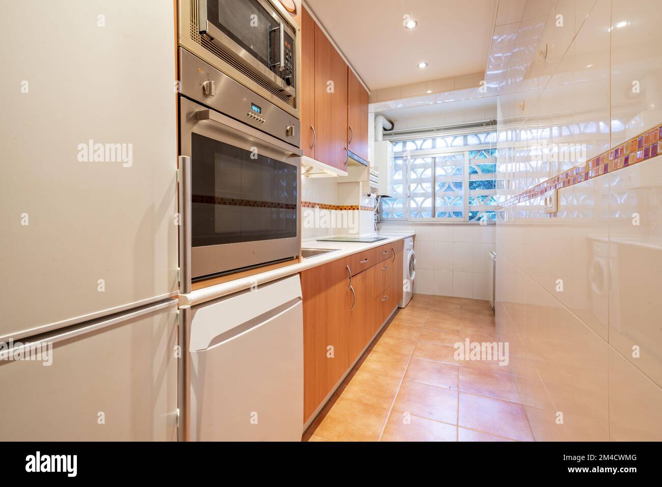 Elongated kitchen with wooden furniture, white countertop and window ...