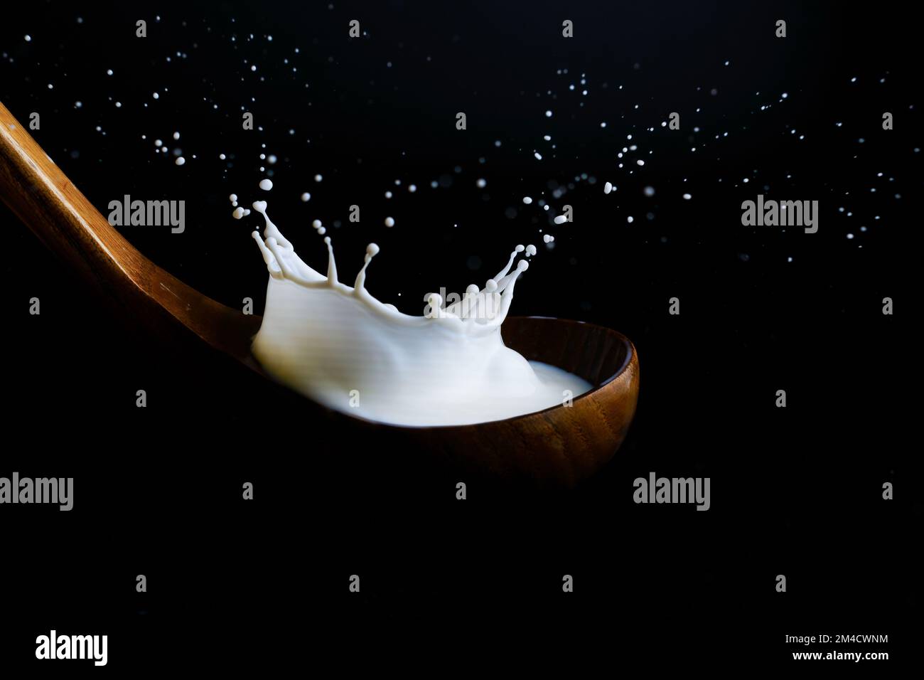 milk splashing on a wooden ladle, with splash effect and black ...