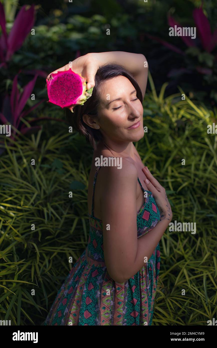A vertical closeup of a beautiful woman holding a dragon fruit in a ...