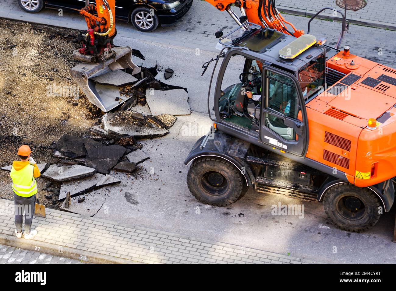 An excavator breaks up the old asphalt layer with a bucket during ...