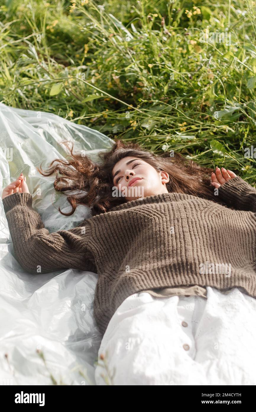 An Asian woman is lying on the ground in a field in a brown sweater ...