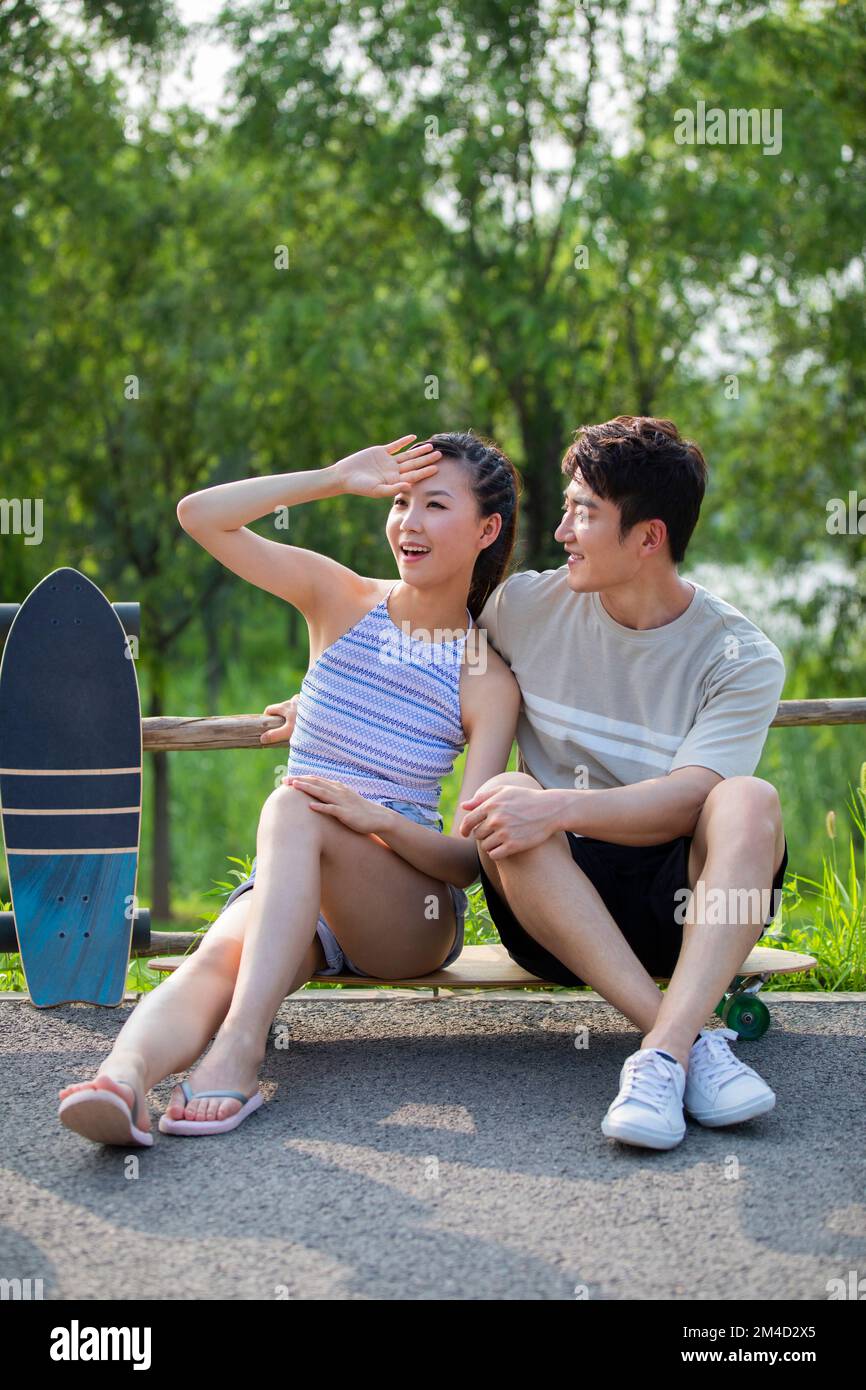 Happy young Chinese couple sitting on a skateboard Stock Photo - Alamy