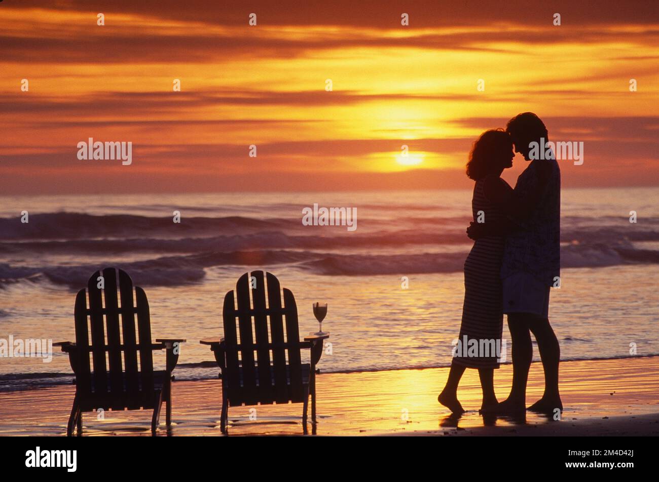 Silhouetted couple standing embracing on the surf against the sunset ...