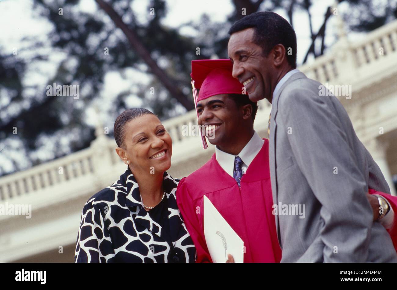 African-American family standing outside while son wears cap and gown ...