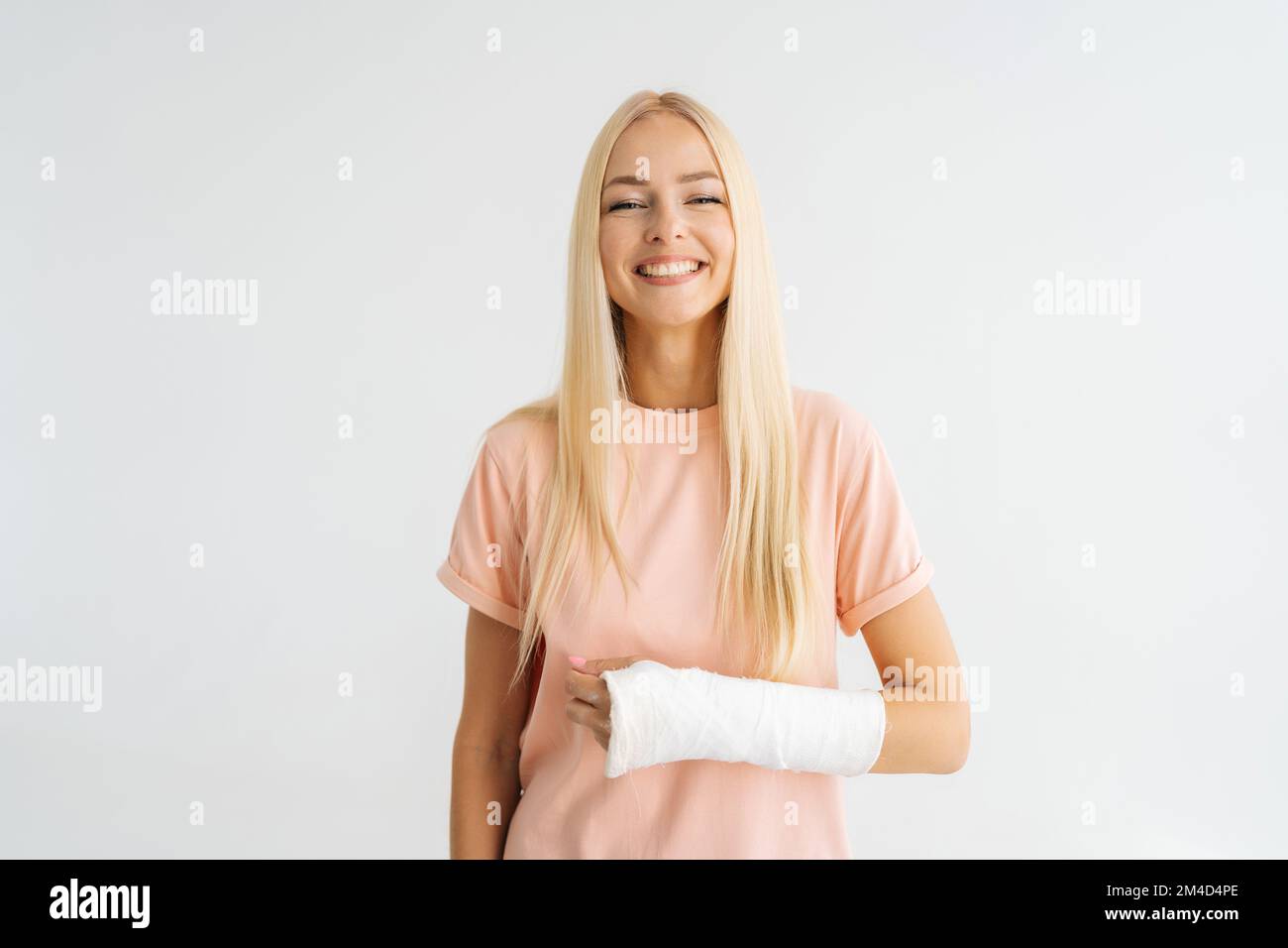Studio portrait of positive blonde young woman with broken arm wrapped ...