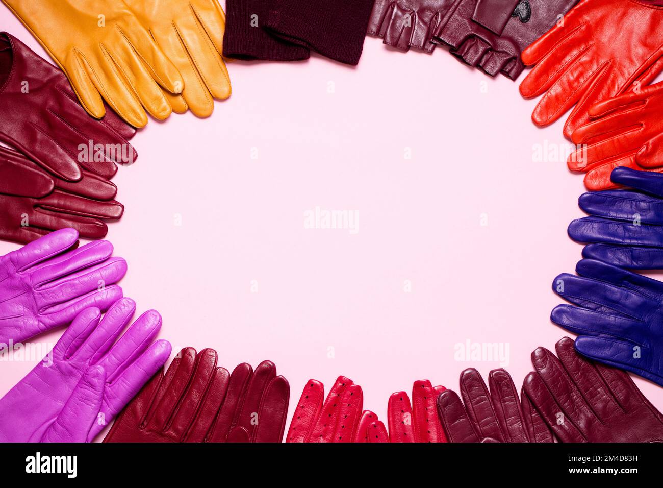Many bright multi-colored gloves are laid out in a circle on a pink ...