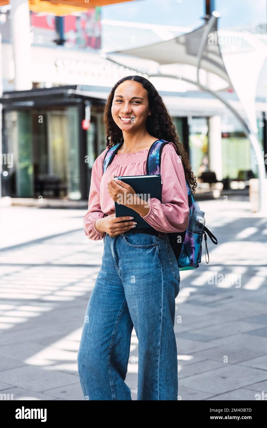 Smiling latin university student woman with a backpack and holding her ...