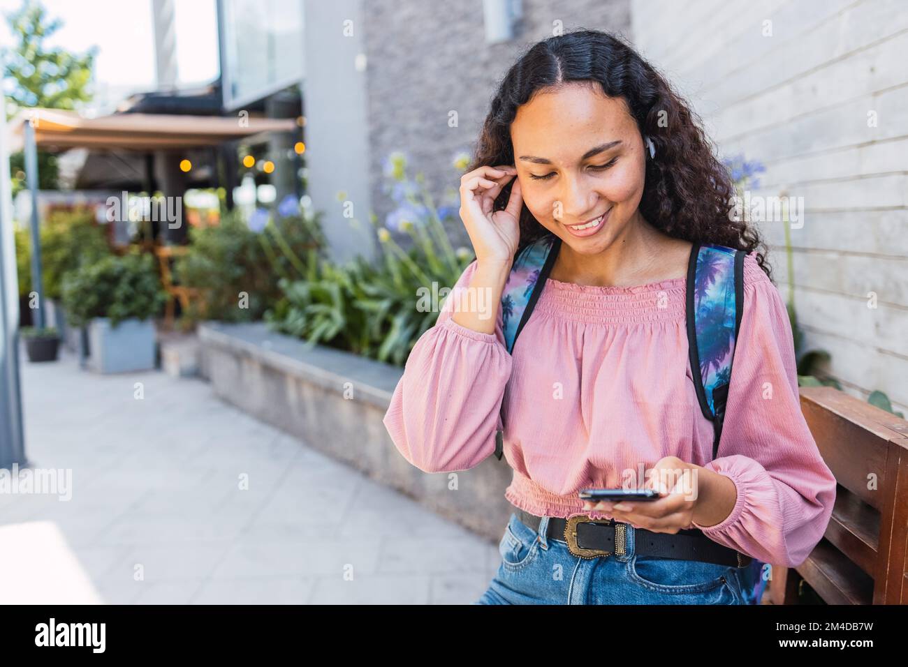 Latin university student woman smiling and using her mobile sitting ...