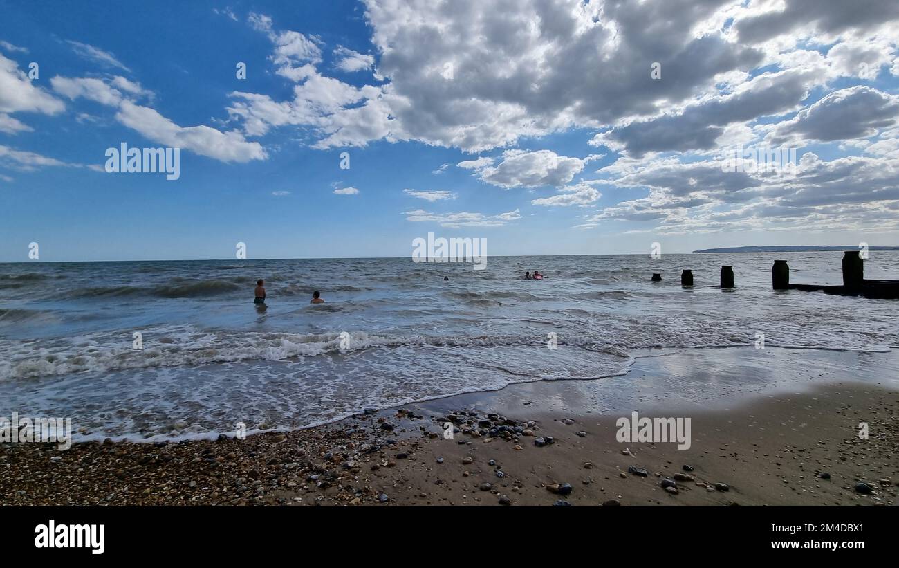 A scenic view of a sea with swimming people under blue cloudy sky Stock ...