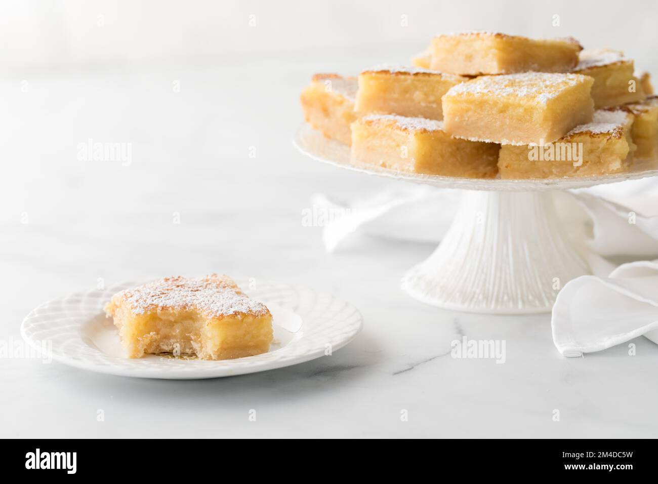 A lemon square with a bite out in front of a stand full of lemon ...