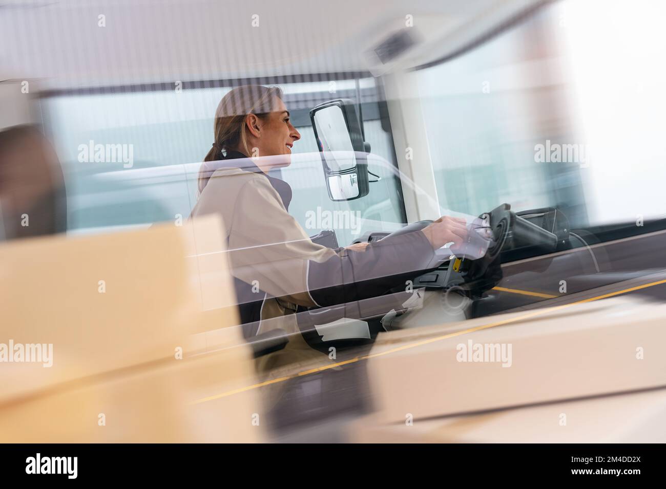 Delivery driver driving van with parcels on seat outside warehouse with ...