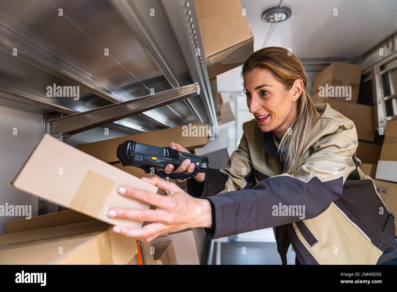 happy female delivery agent scanning barcode inside her van on a parcel ...