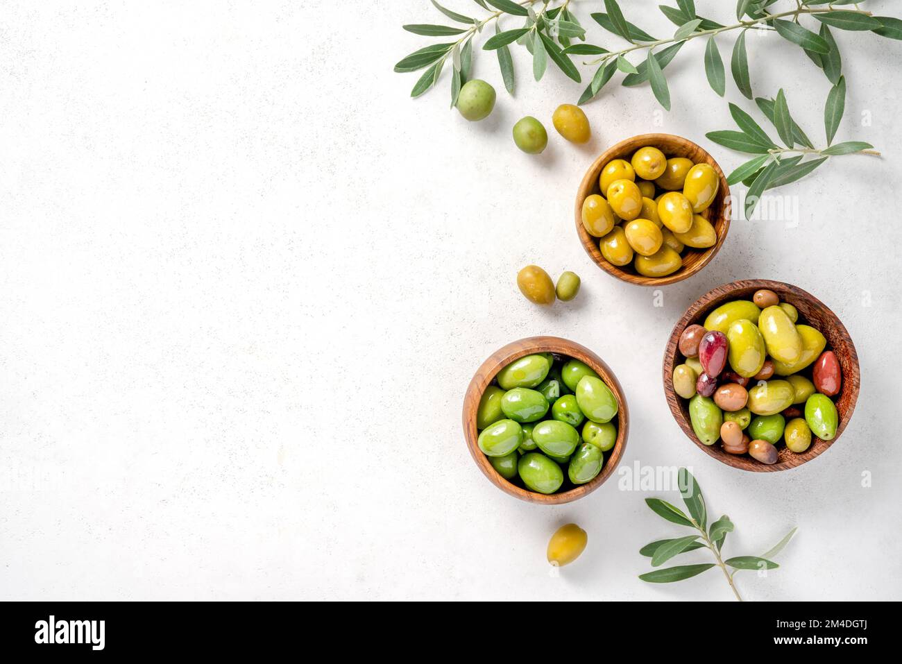 Different olives in bowls on white concrete background. Top view of ...