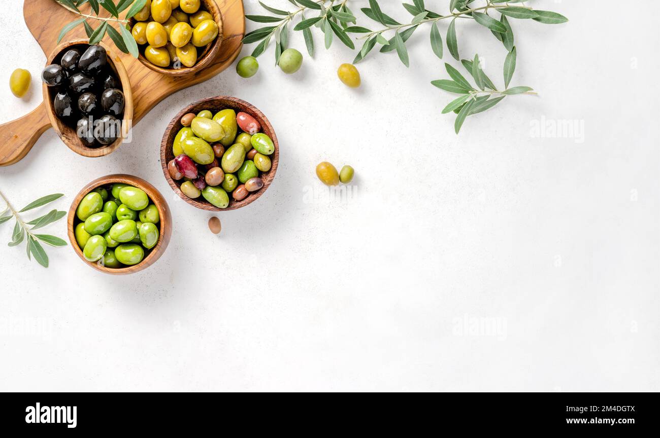 Different olives in bowls on white concrete background. Top view of ...