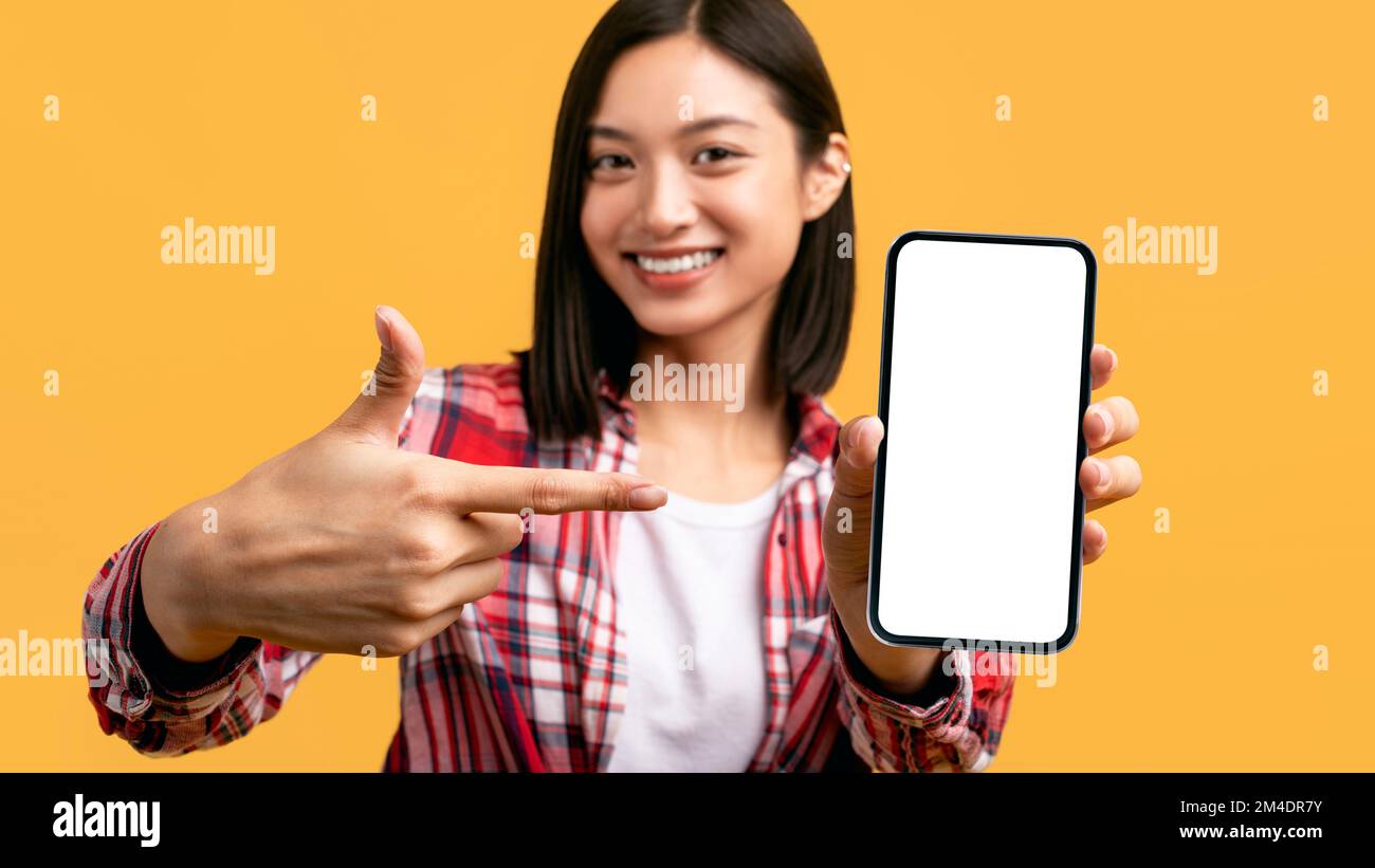 Mobile app. Happy asian lady pointing at cellphone with blank screen ...