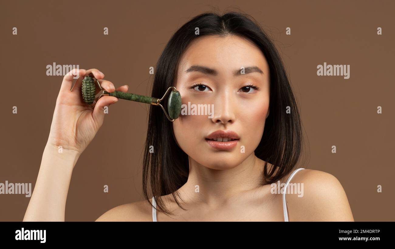 Beautiful japanese lady using greenstone jade facial roller for skin ...