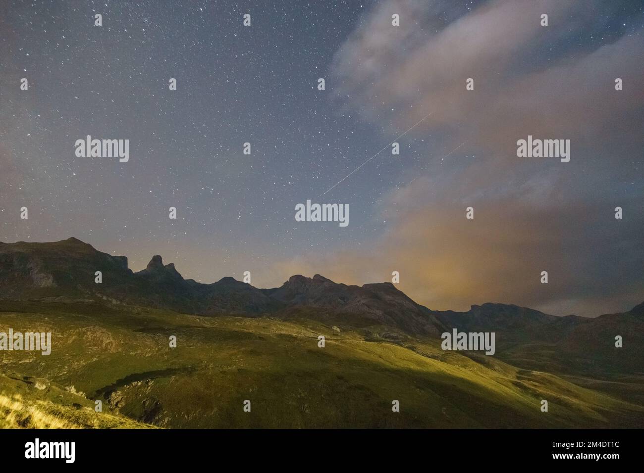 Night sky with stars over an illuminated meadow of the Pyrenees ...