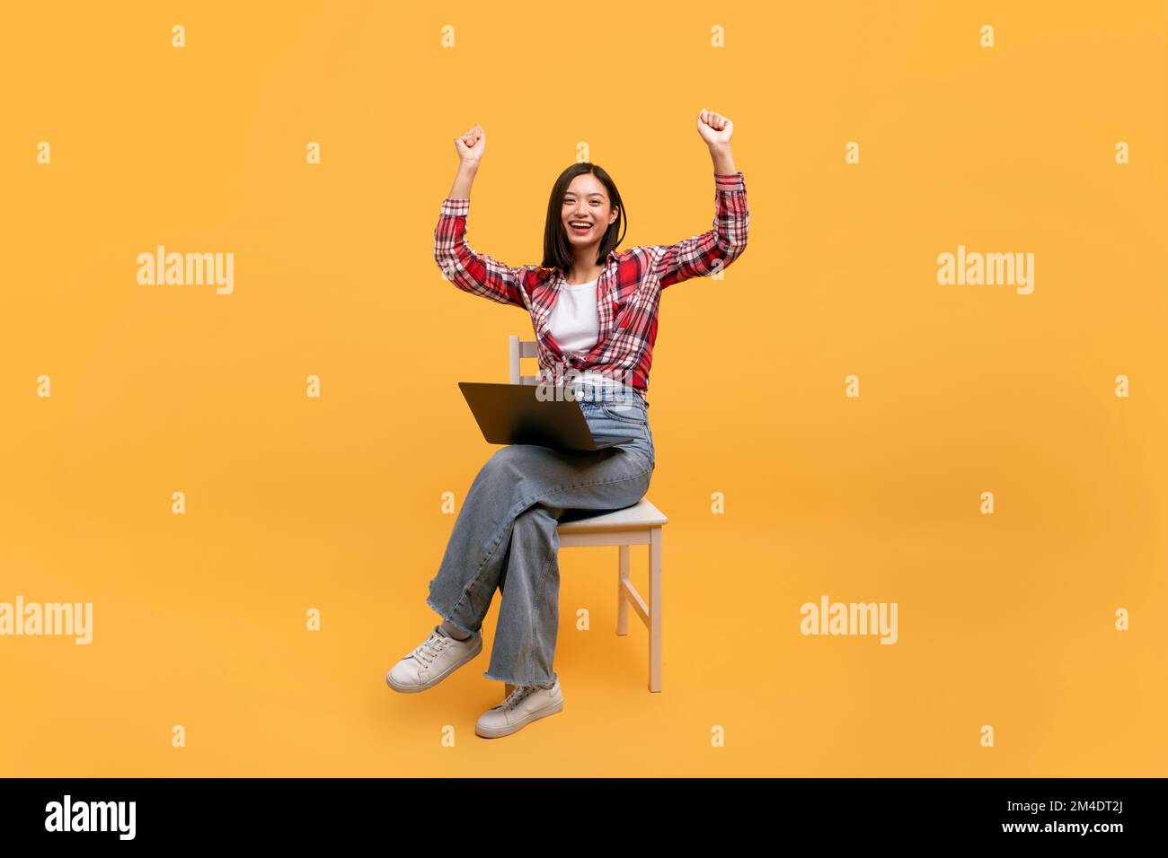 Big win, amazing online offer. Overjoyed asian lady sitting on chair ...