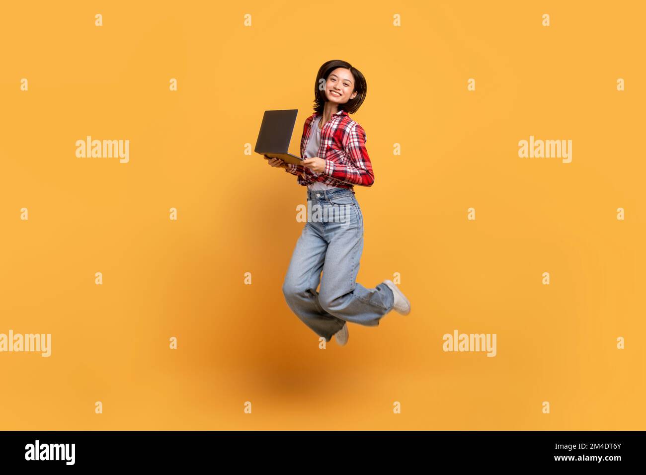 Full body length of happy asian lady jumping and holding pc laptop ...