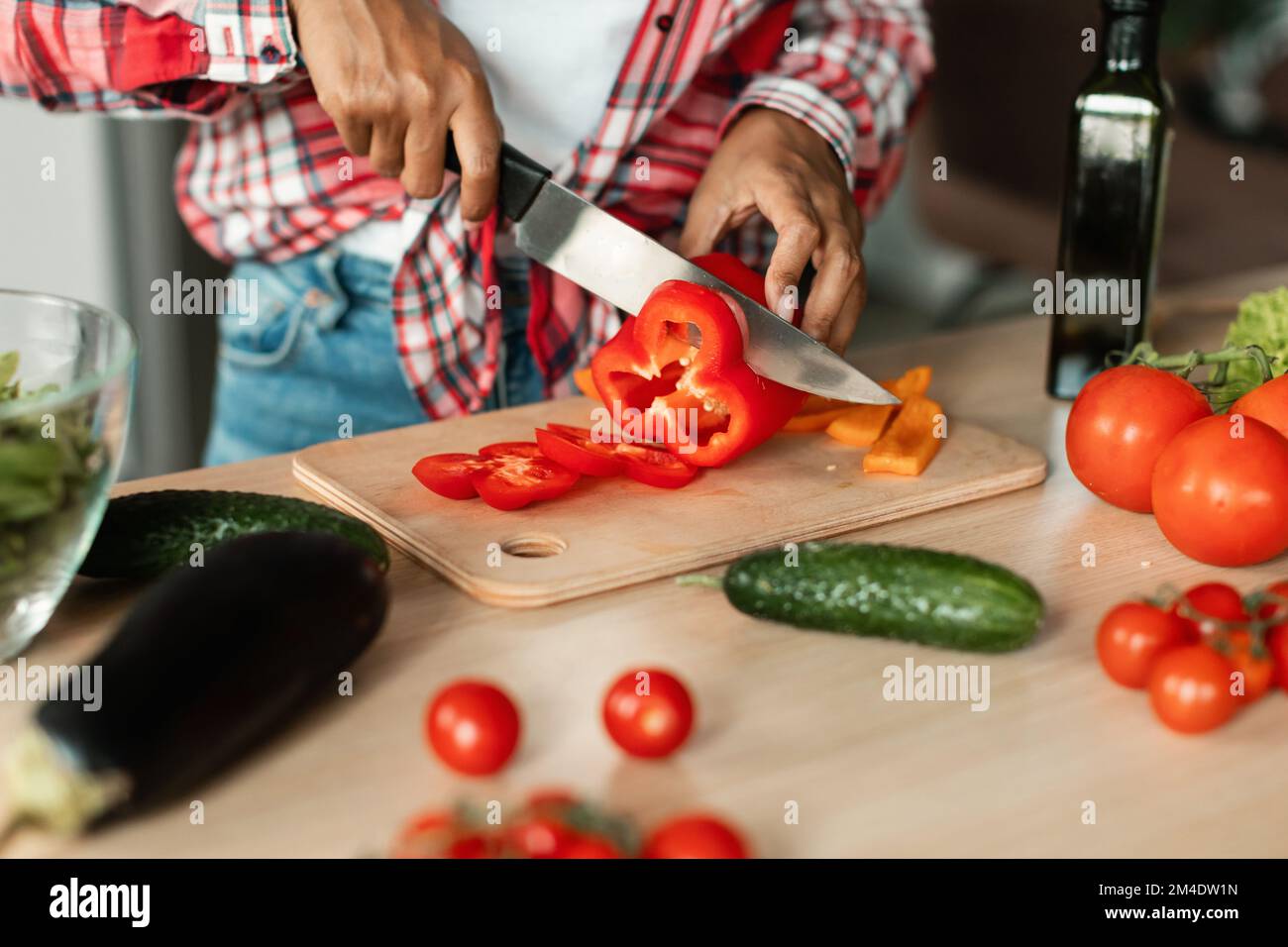 Millennial black female chef preparing salad, cut pepper, prepare lunch ...