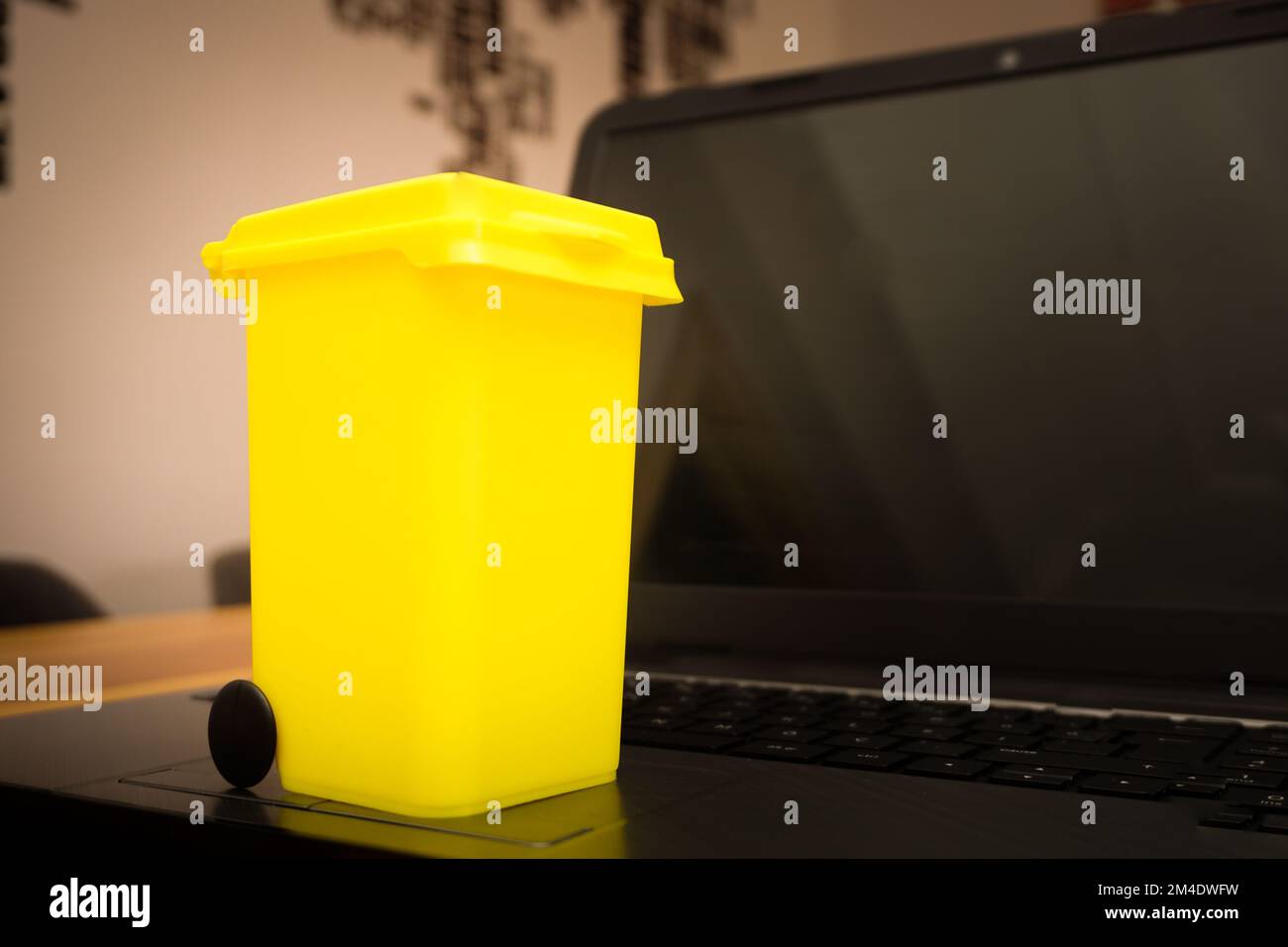 A miniature yellow bin on a laptop representing electronic waste ...