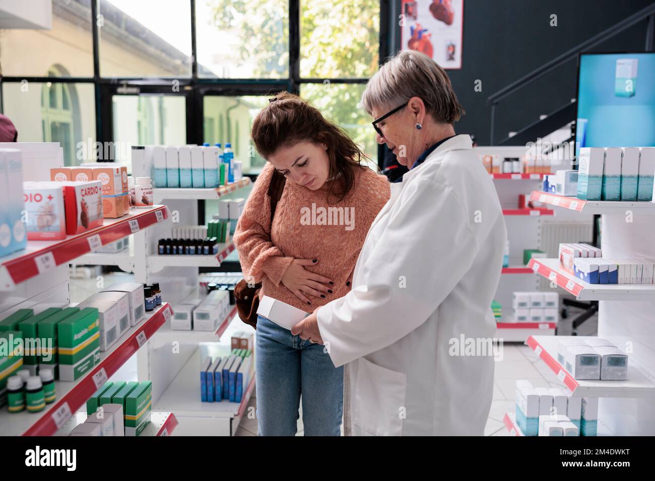 Woman customer suffering from stomachache asking pharmacist about pills or painkillers to cure ...