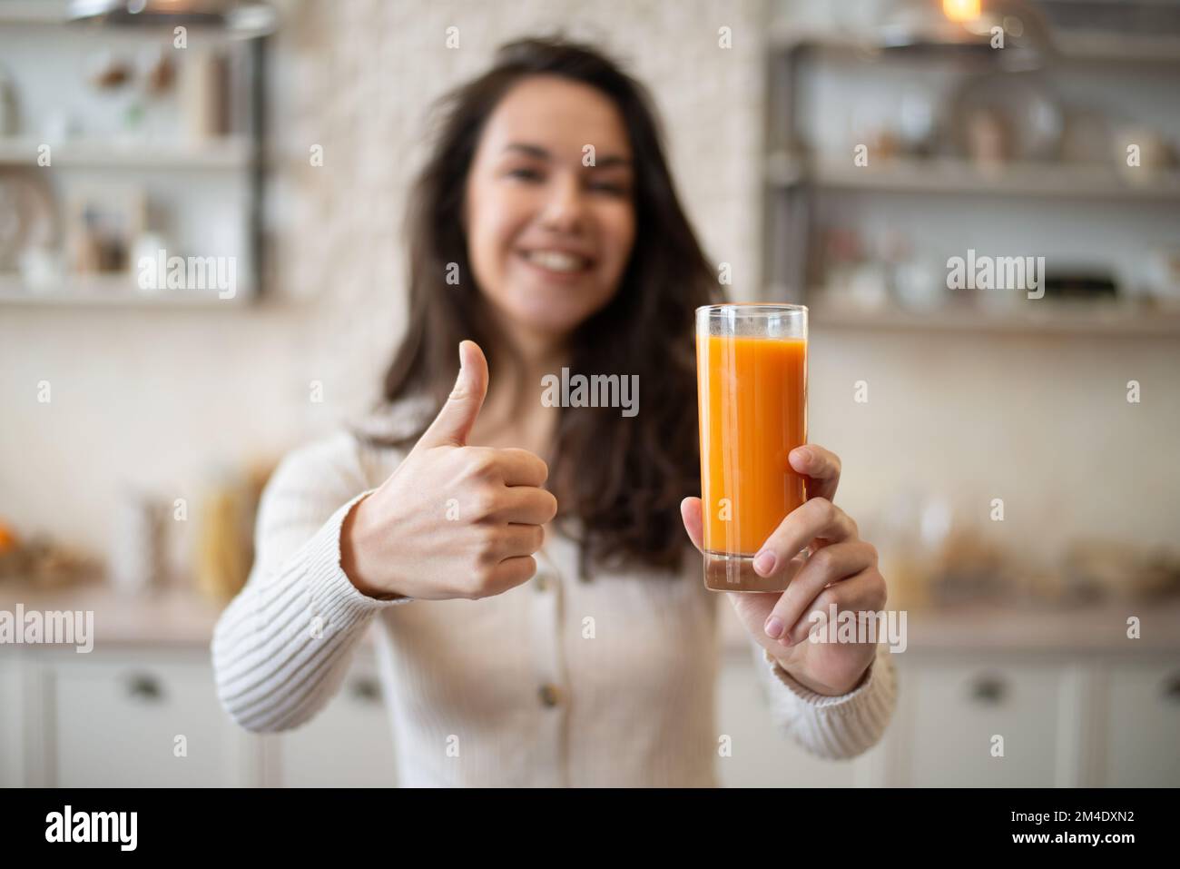 Positive caucasian lady holding glass of organic orange juice and ...