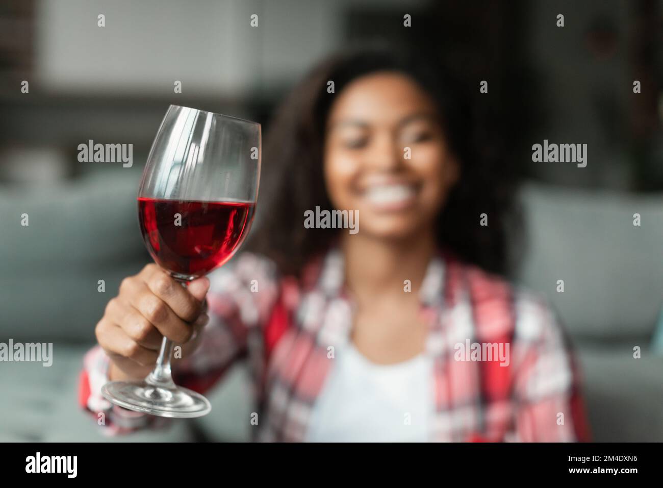 Smiling Millennial Black Lady Cheers Glass Of Wine To Camera In Living