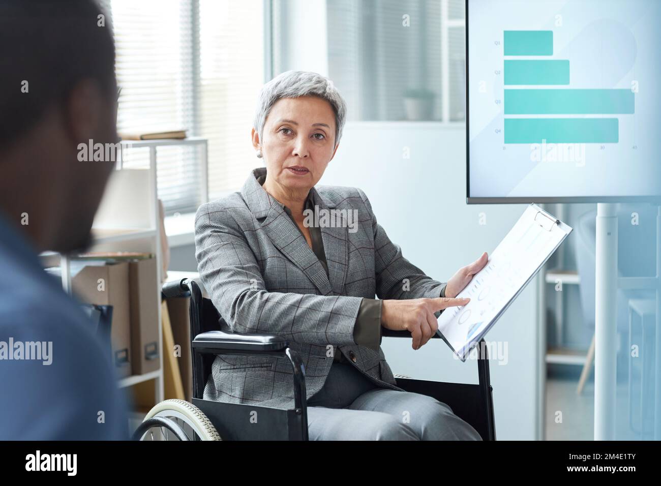Portrait of senior woman using wheelchair while giving presentation in ...