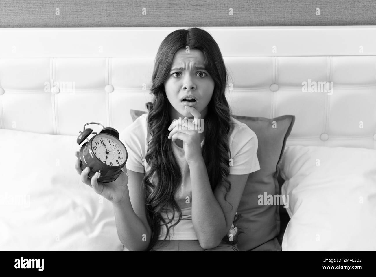 This clock is slow. Anxious kid hold alarm clock. Being upset by ...