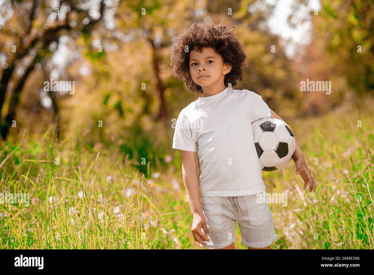 Curly-haired boy in white sportswear with a football Stock Photo - Alamy