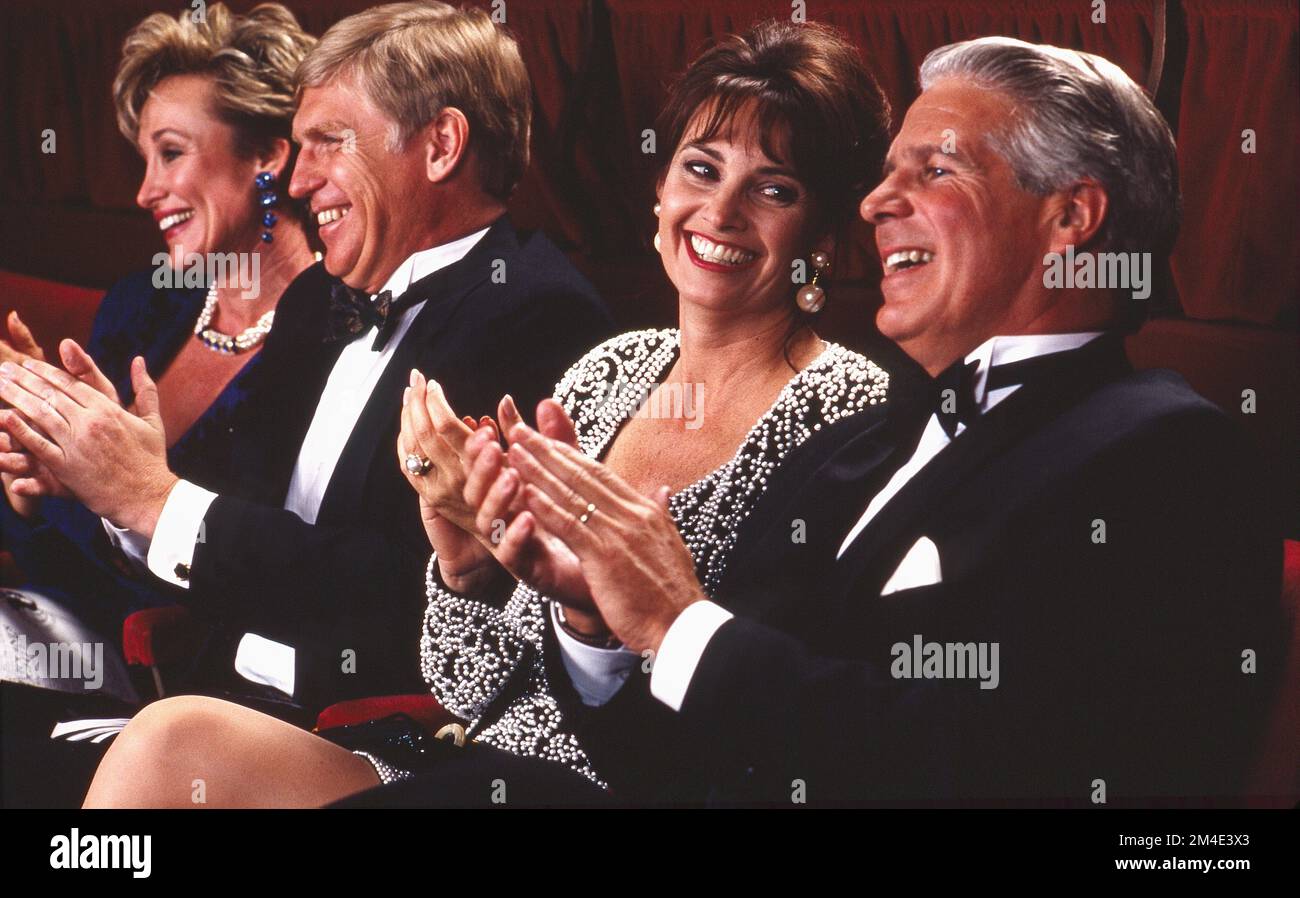 Two older couples in formal attire clapping and laughing while at a ...