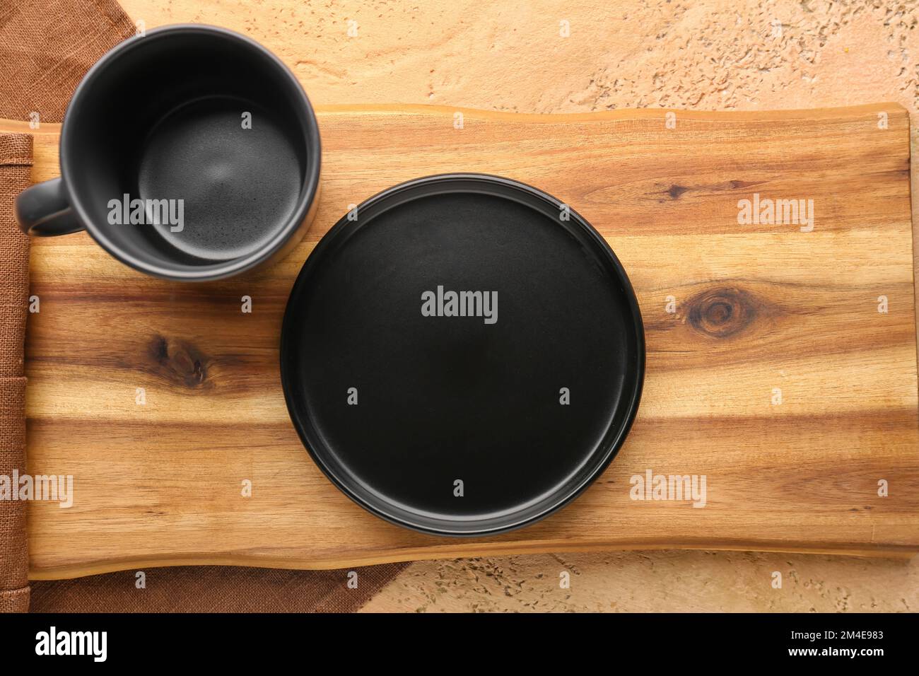 Wooden board with black plate, cup and brown napkin on grunge beige ...