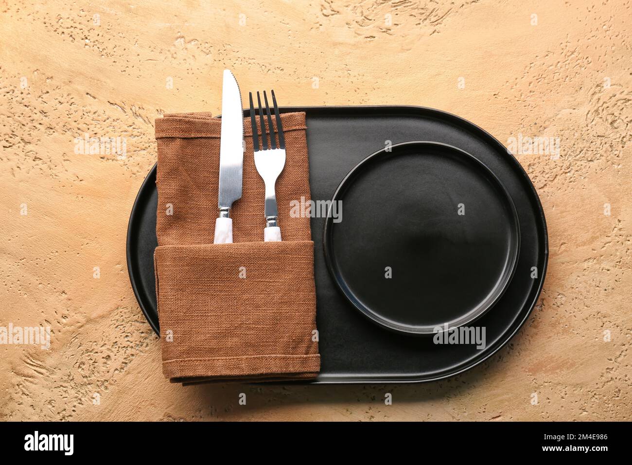 Black plate on tray with cutlery in brown napkin on grunge beige ...