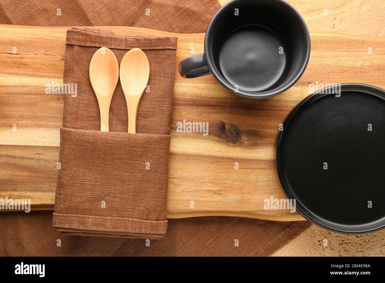 Wooden board with black plate, cup and spoons in brown napkin on grunge ...