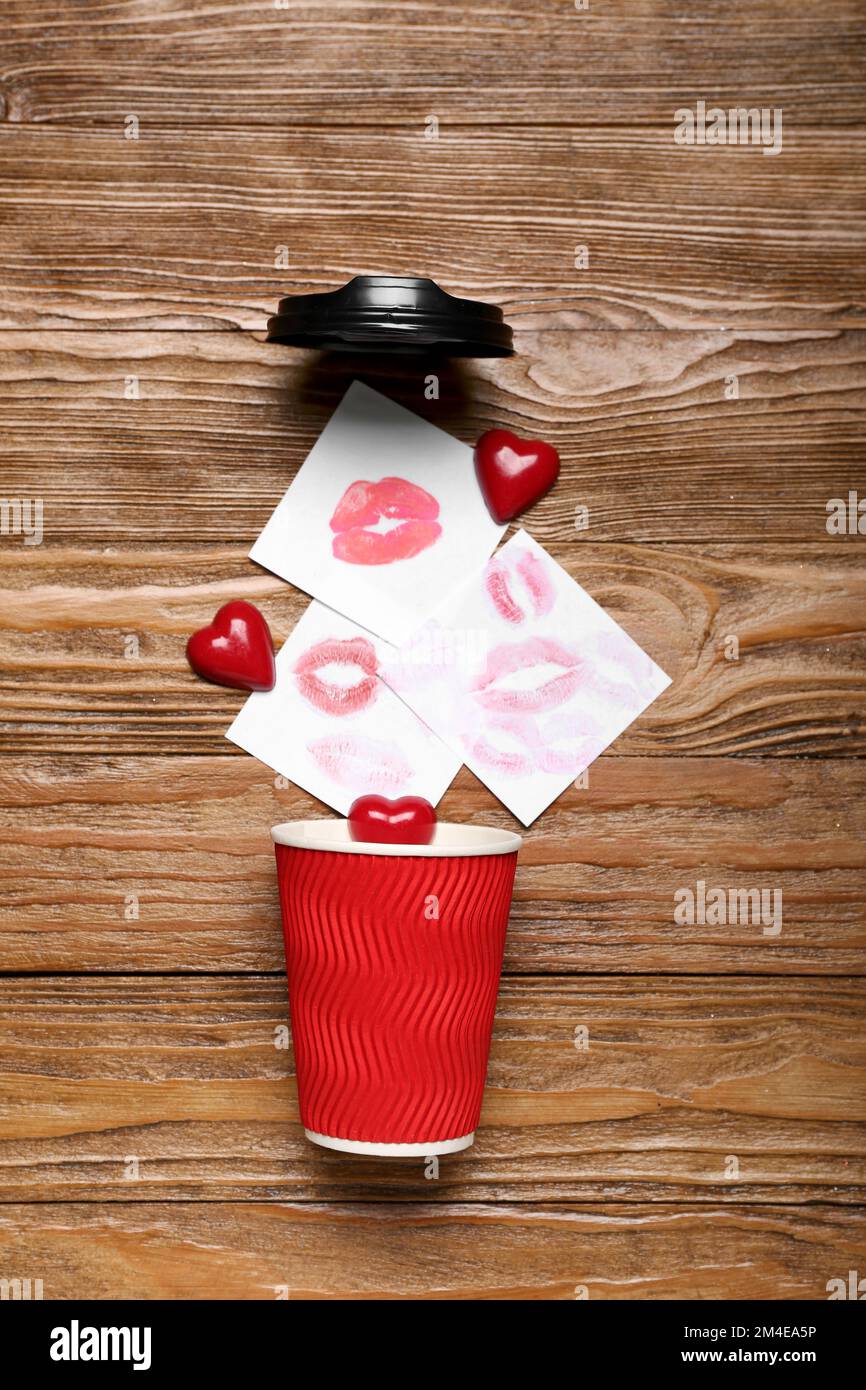 Takeaway cup with candies and lipstick kisses on wooden background ...