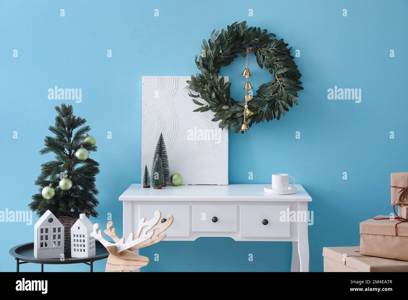 Table with painting, Christmas wreath, fir trees and cup near blue wall ...