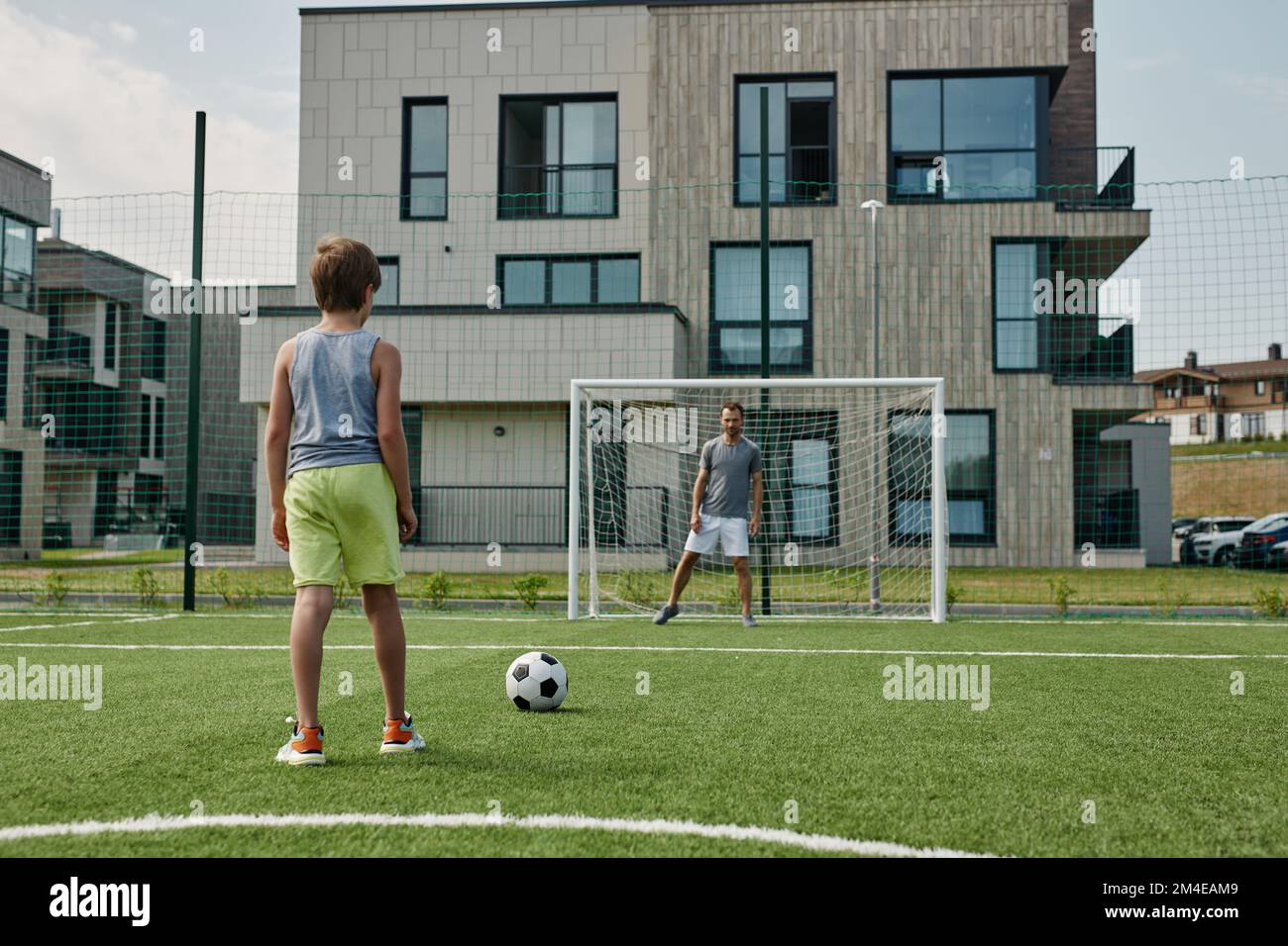 Back view of teenage boy playing football with father standing in gates ...