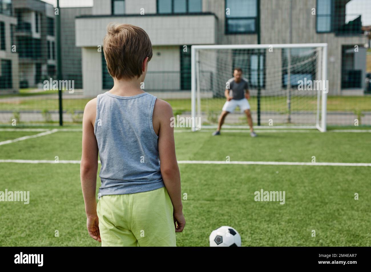 Back view of young boy playing football with father standing in gates ...