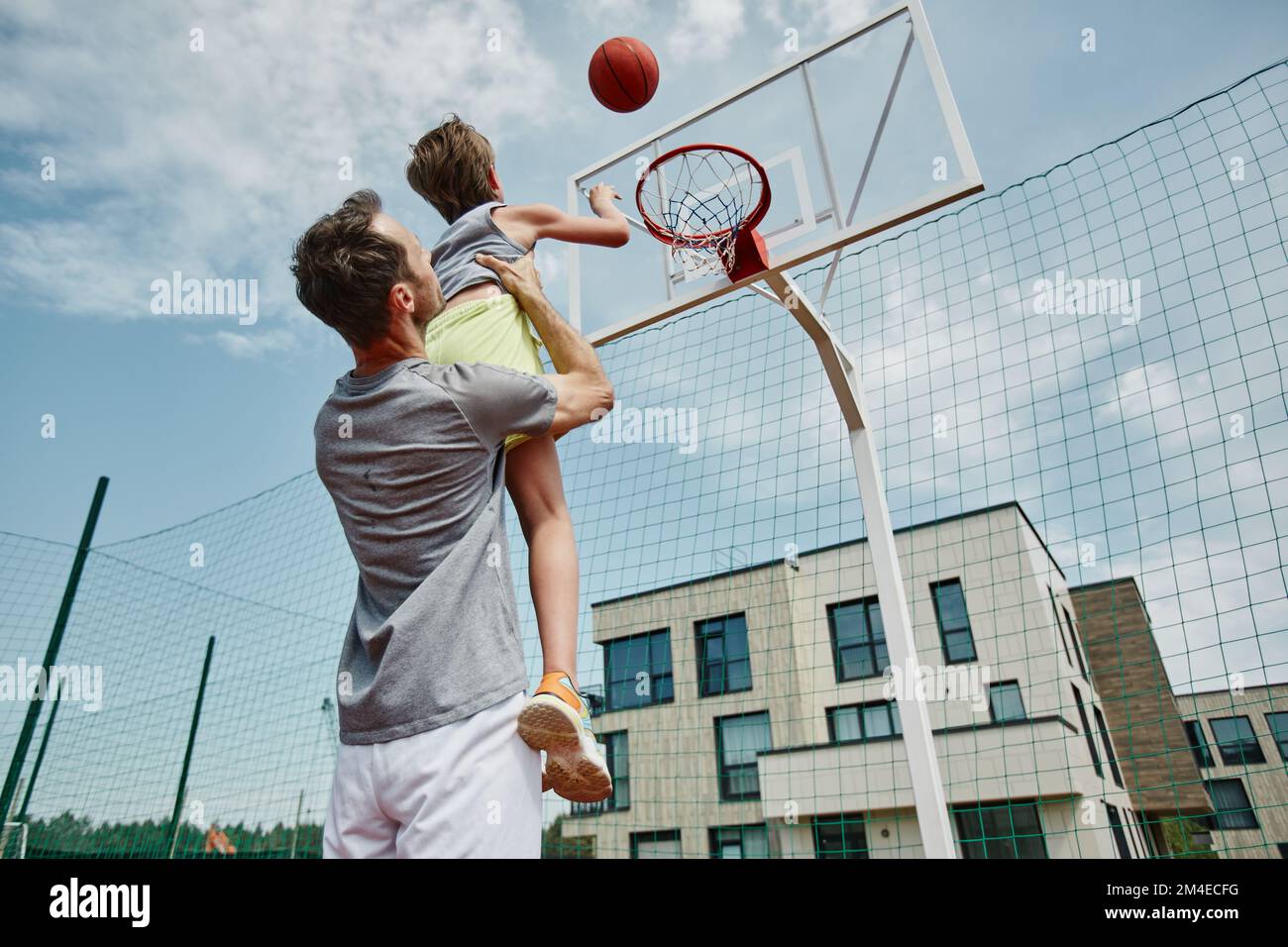 Low angle portrait of father and son playing basketball together, man ...
