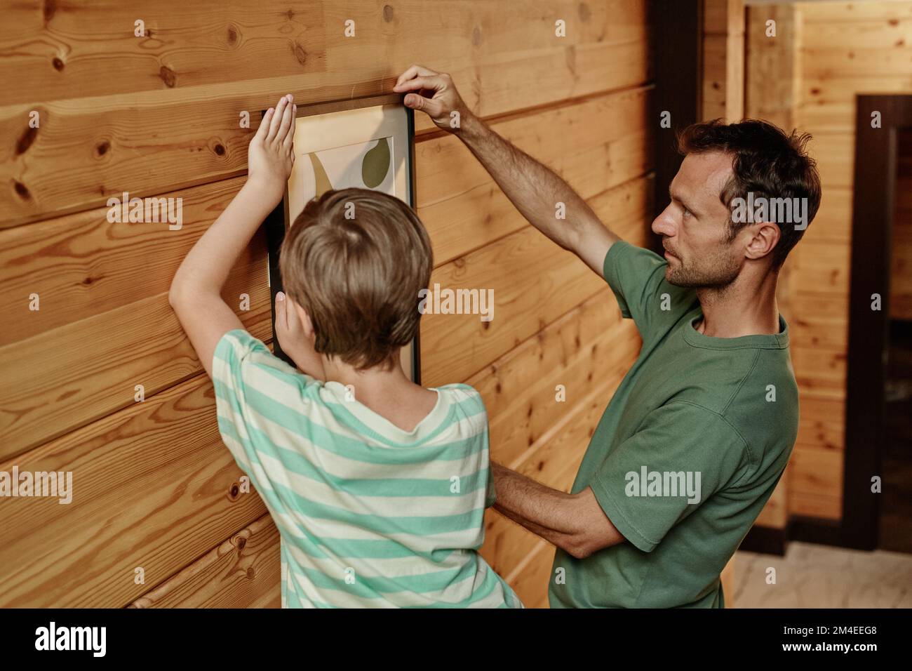 Side view portrait of father and son hanging picture on wooden wall in ...