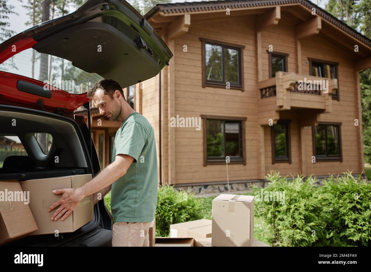 Side view portrait of young man unloading boxes from car trunk while ...