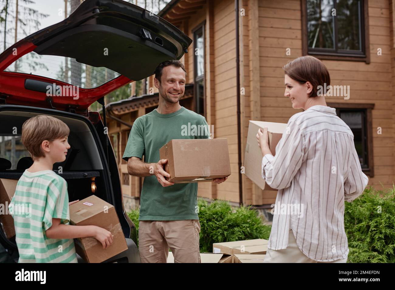 Portrait of happy family unloading boxes from car trunk while moving ...