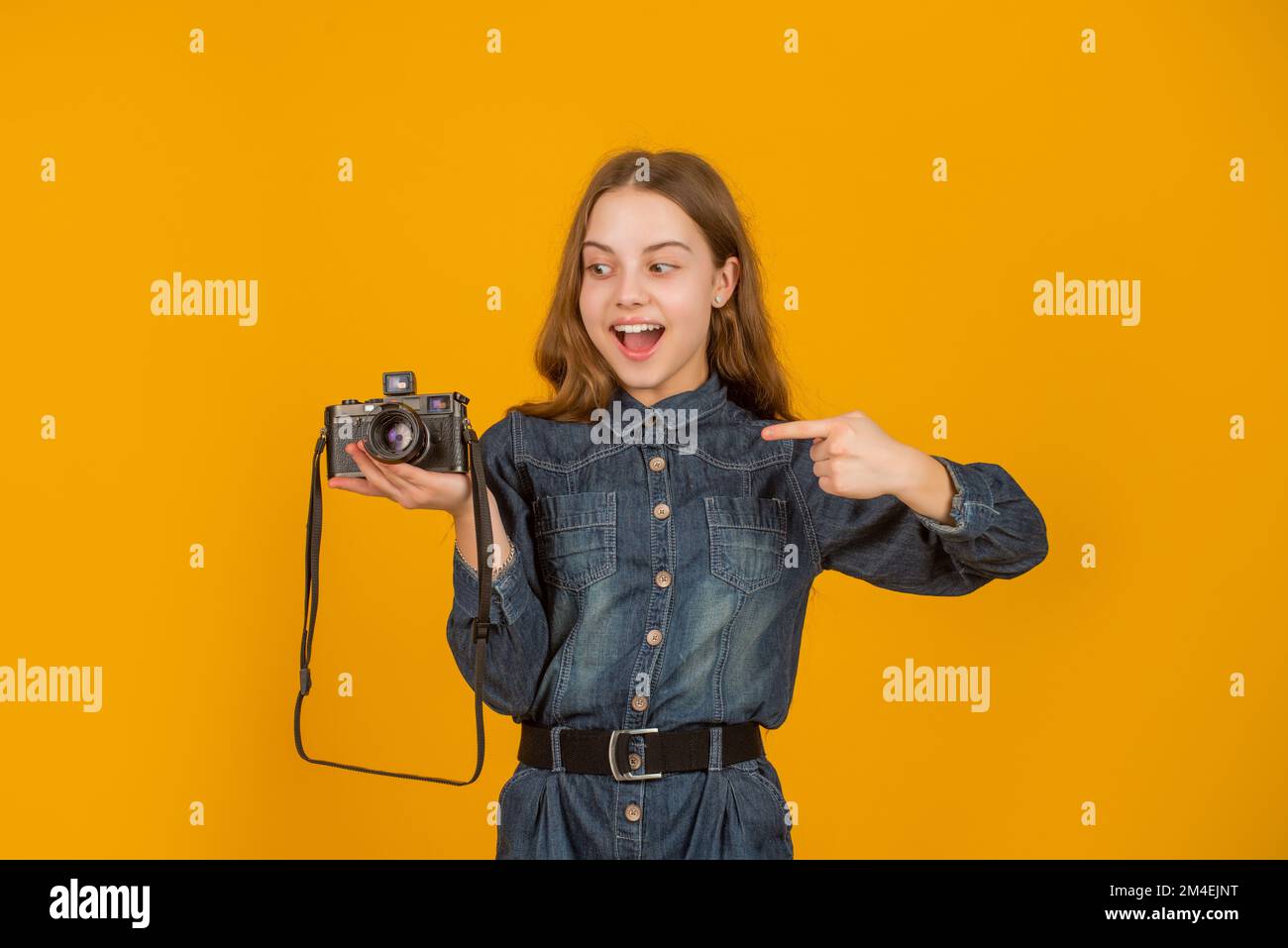 Surprised teen photograper pointing finger at photo camera yellow ...