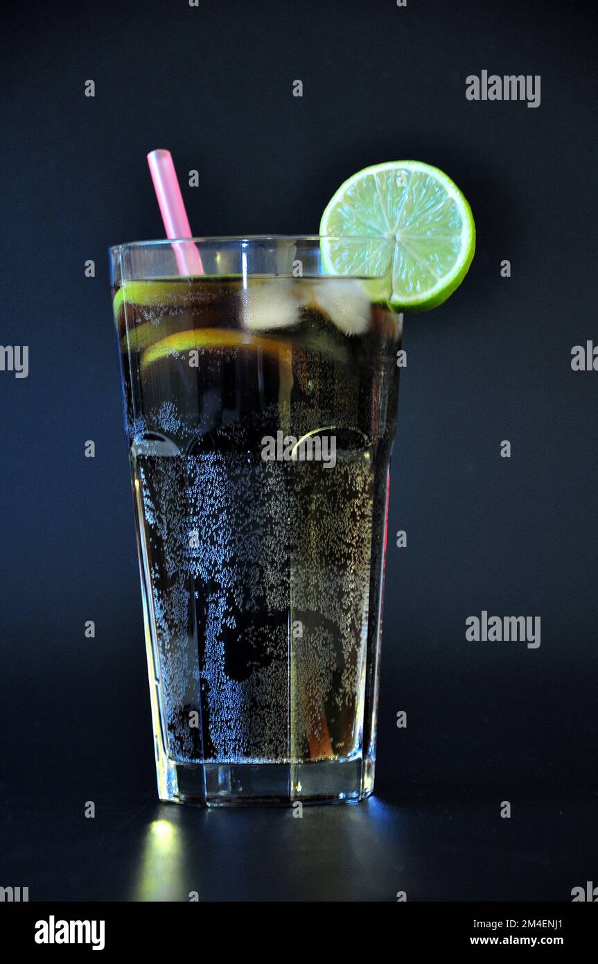 Cola with lime, a refreshing soft drink with ice and a straw in a tall glass on a black ...