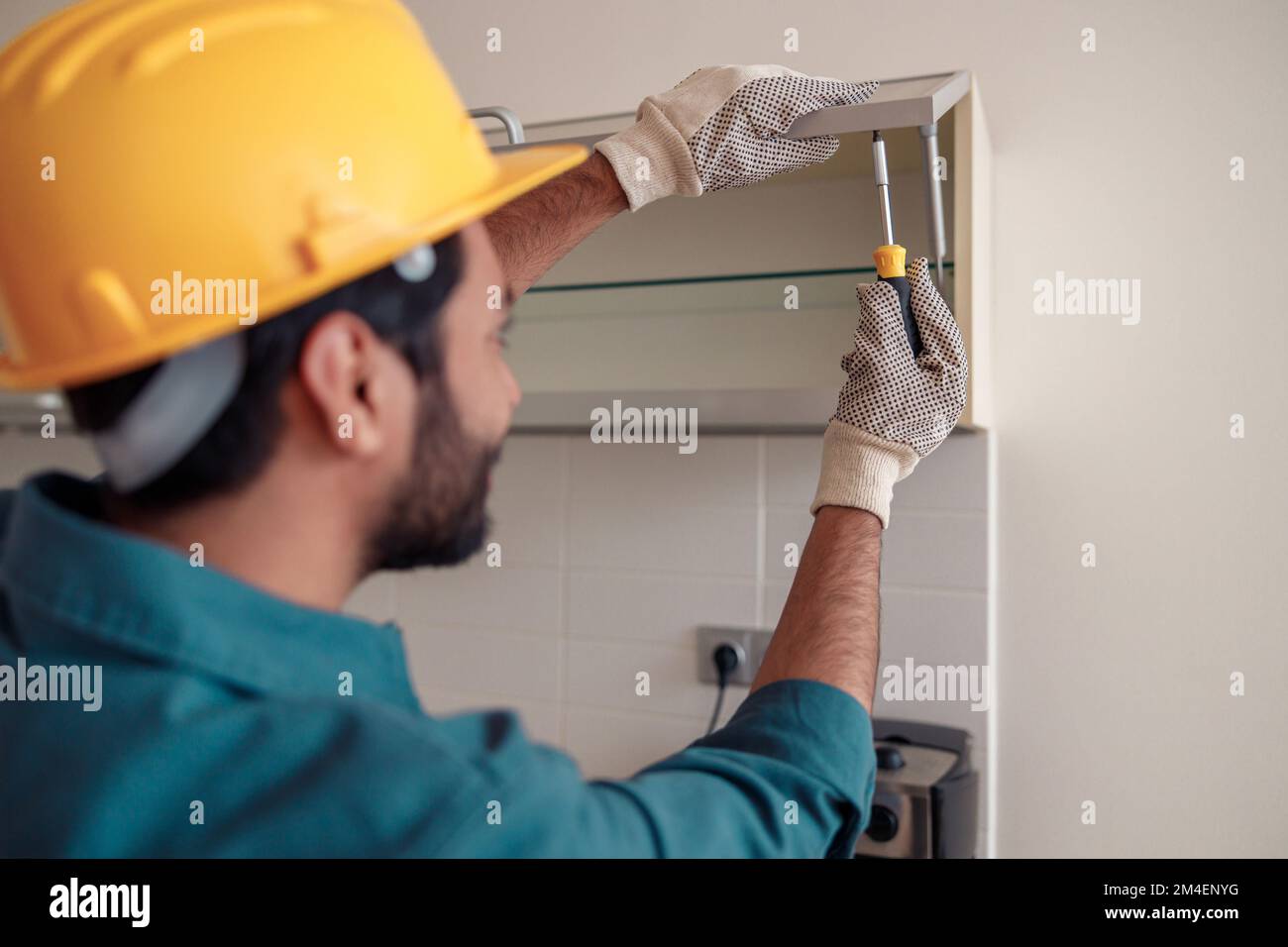 Back view of worker in uniform is assembling furniture on kitchen ...
