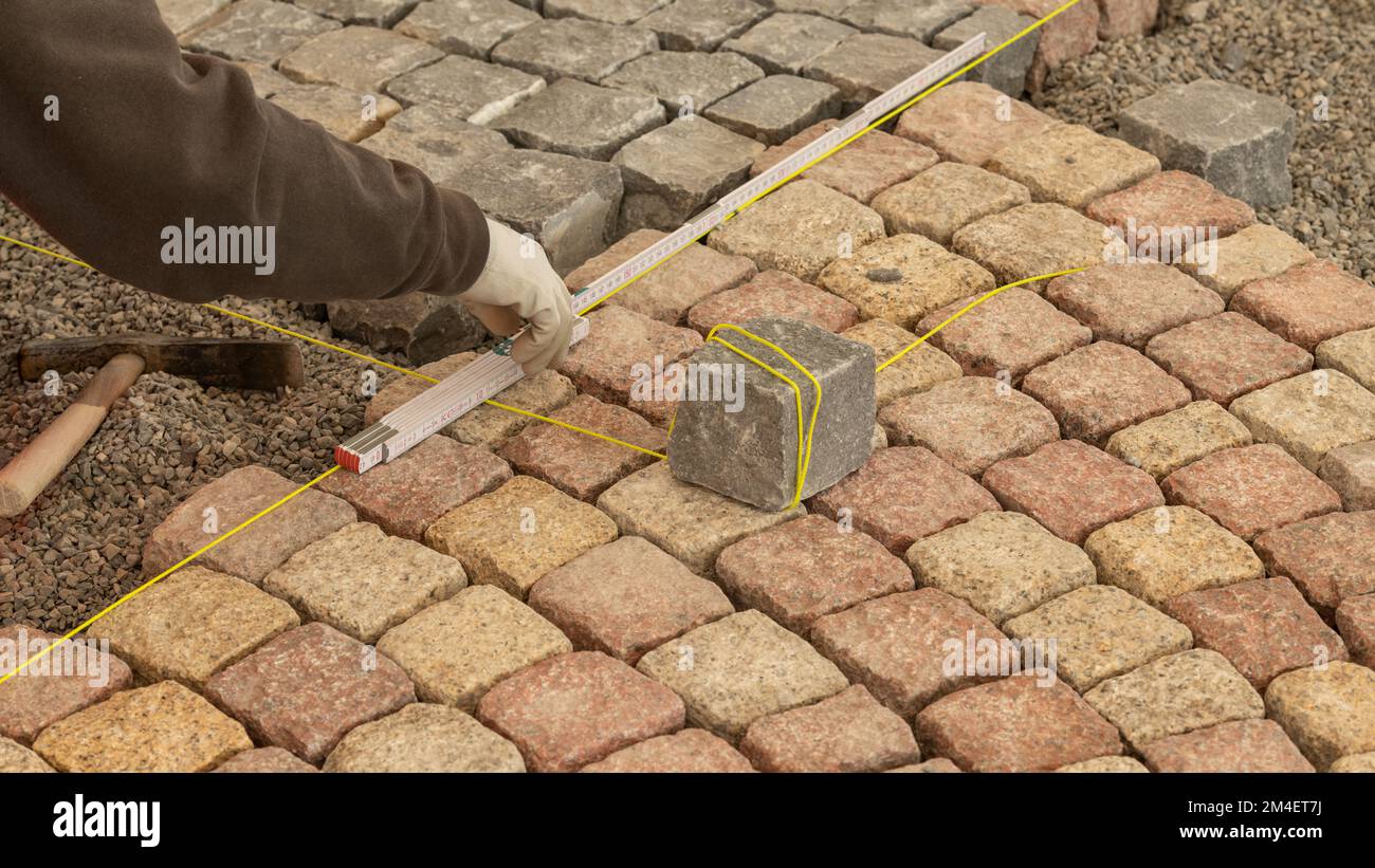 A closeup of a worker measuring a bar of sidewalk tiles for the final ...