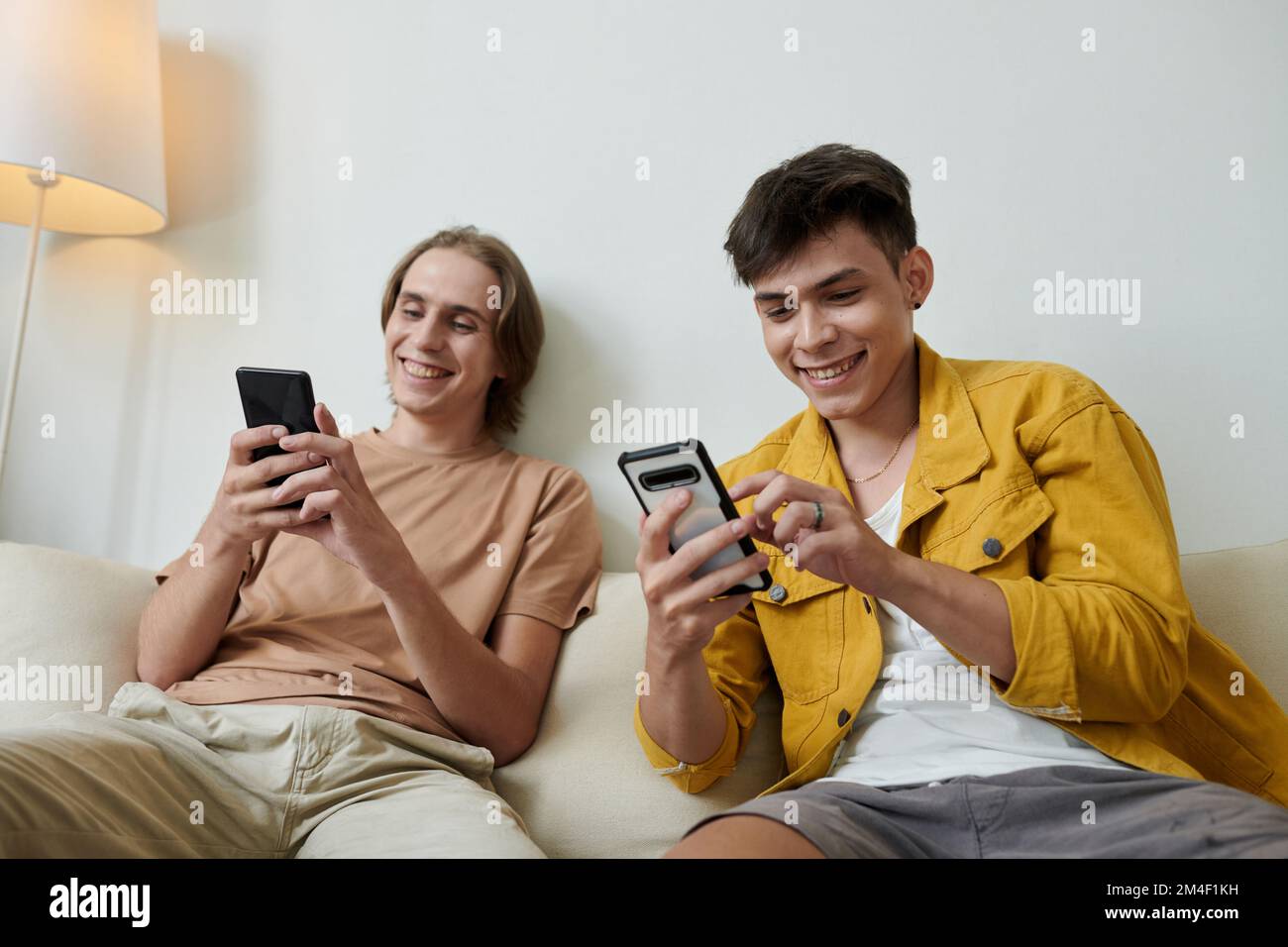 Joyful young men texting friends when sitting on couch at home Stock ...