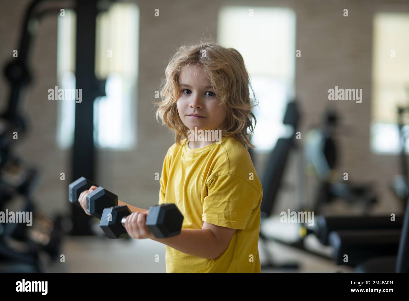 Kid workout kid in gym. Sport activities at leisure with children. Blonde boy holding dumbbells ...